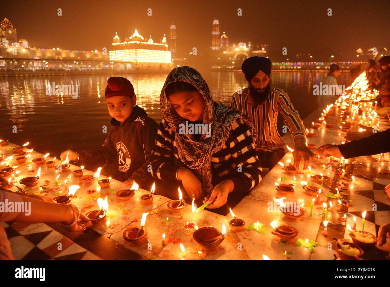 Sikh devotees light clay lamps next to the pond surrounding the Golden ...