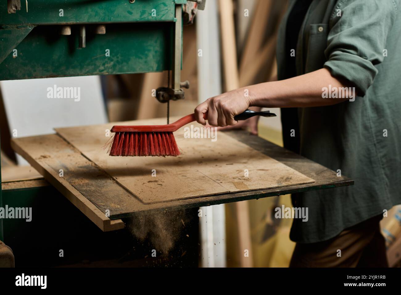 A skilled carpenter cleans up wood shavings with a broom, focused on ...