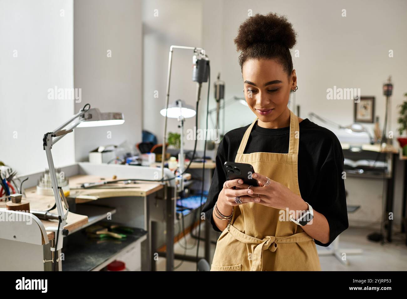 A skilled woman in an apron uses her smartphone in her artistic, tool filled workspace Stock ...
