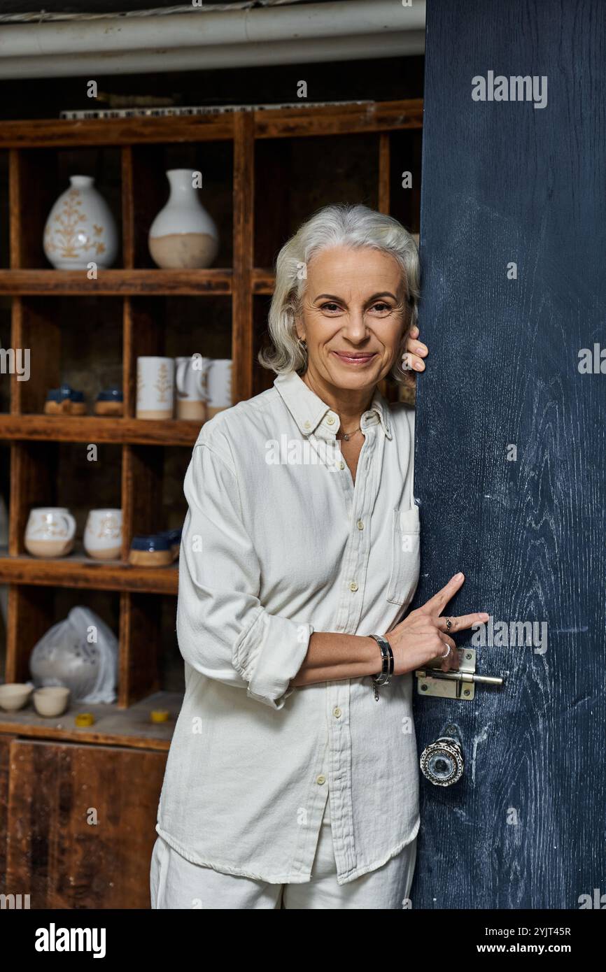 A cheerful woman stands at the doorway of her pottery studio, inviting ...