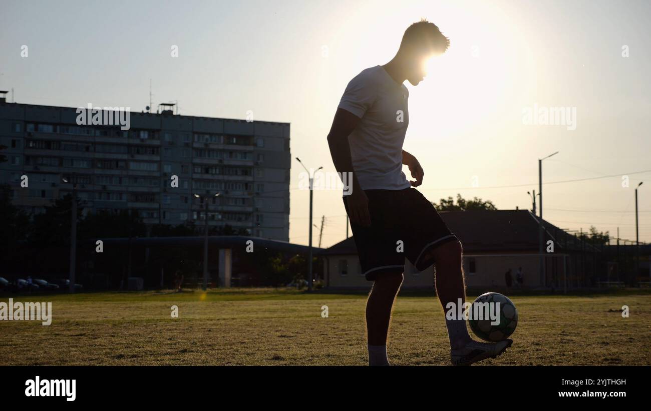 Professional footballer juggling soccer ball on stadium at sunset ...
