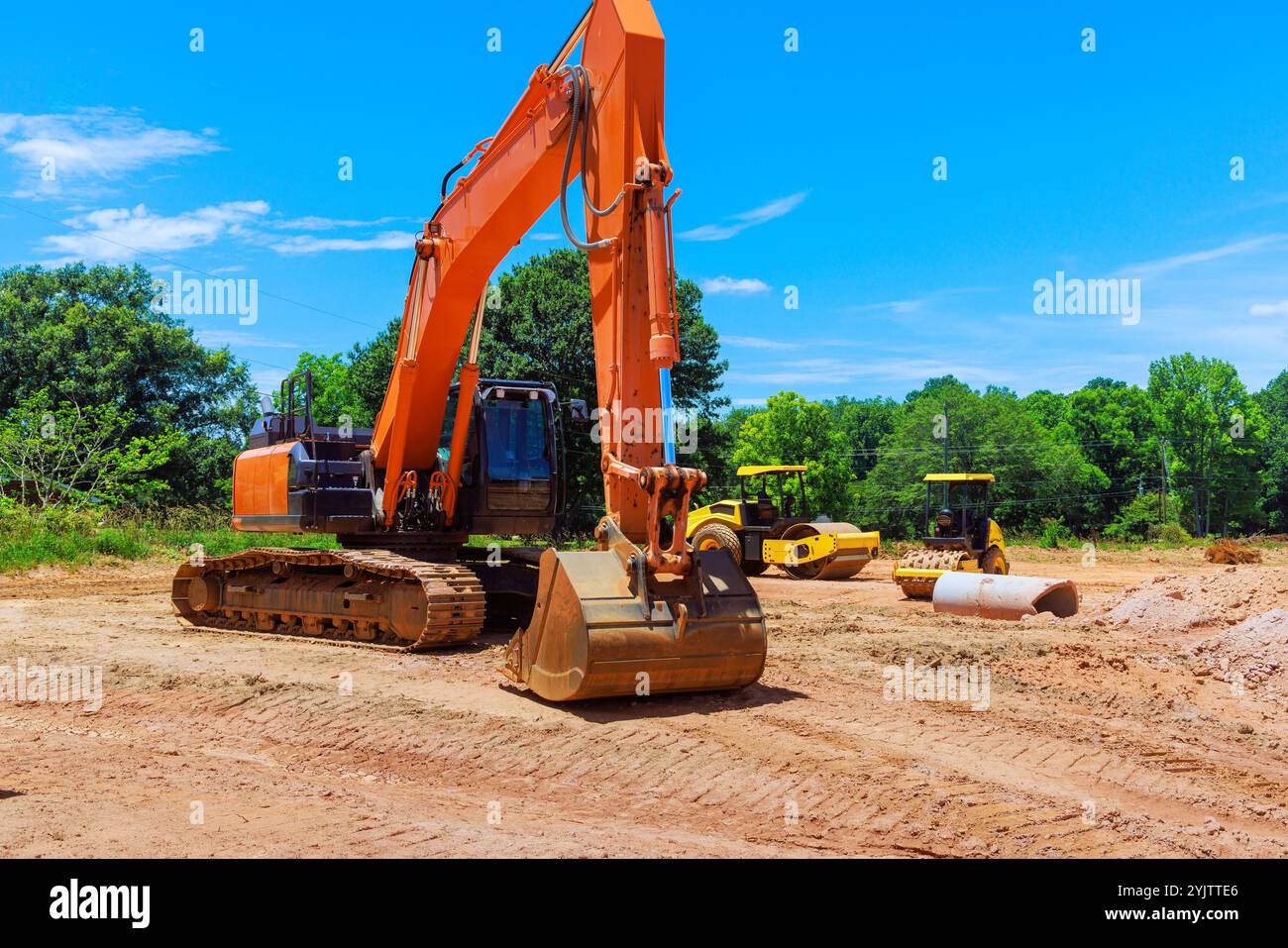 An excavator is digging into earth while two road rollers are preparing ...