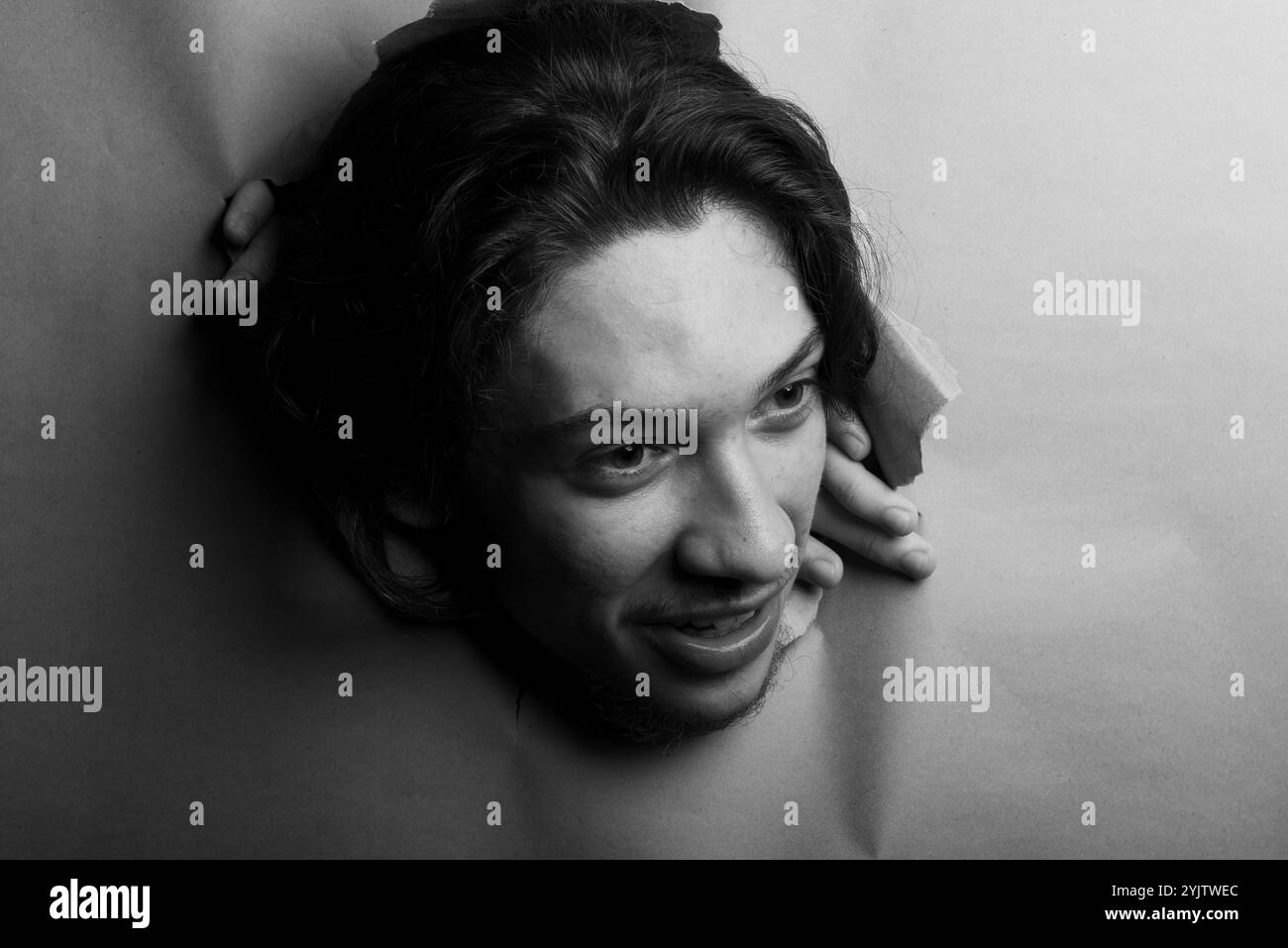 Man head sticking out and looking through a paper hole with his hands ...