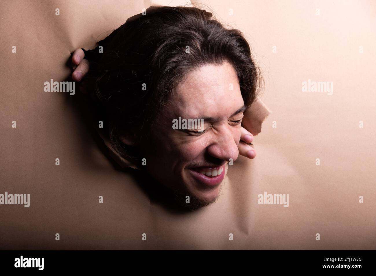 Man head sticking out and looking through a paper hole with his hands ...