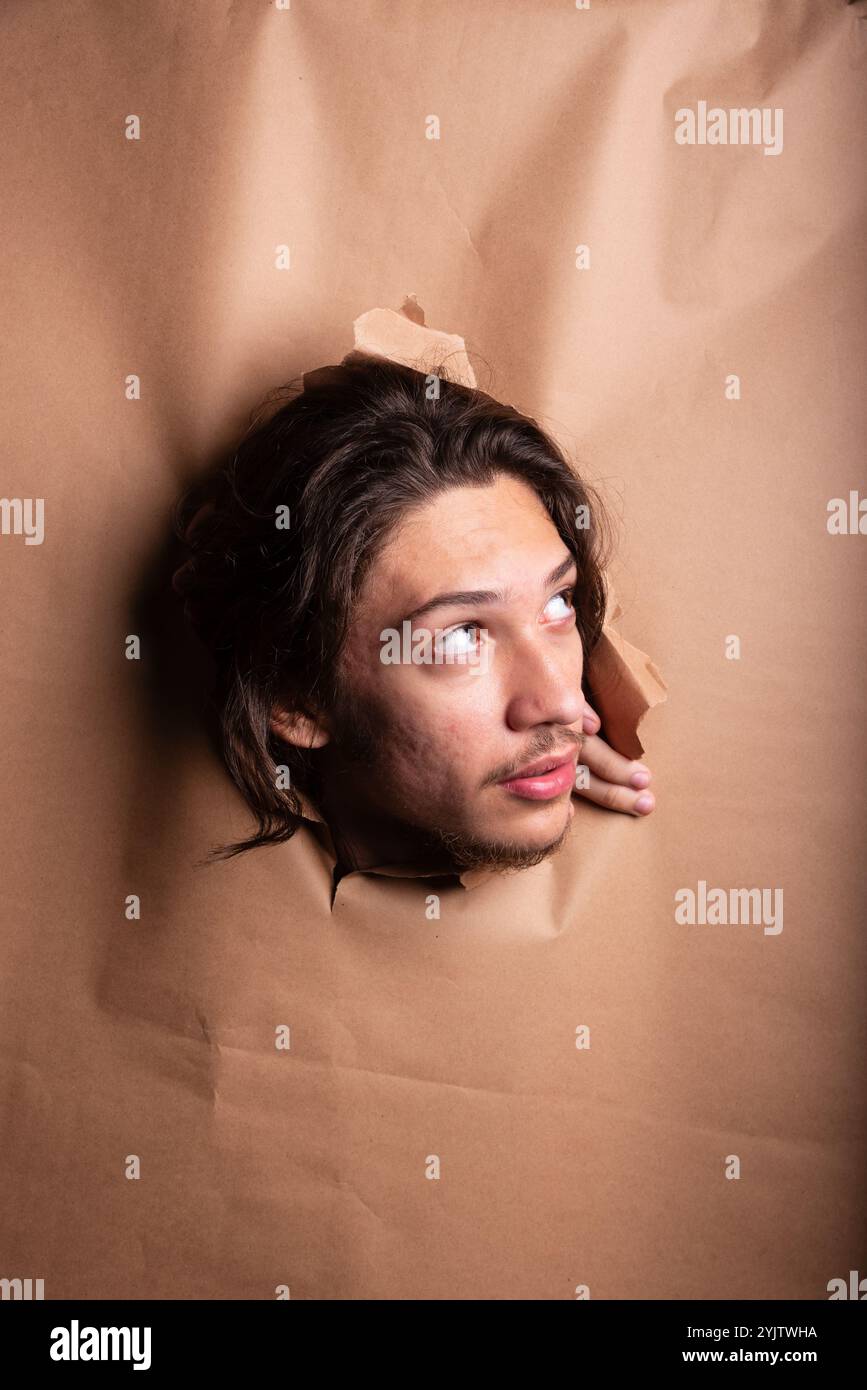 Man head sticking out and looking through a paper hole with his hands ...
