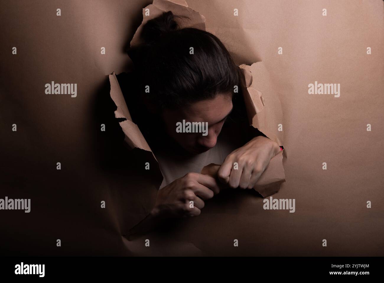 Man head sticking out and looking through a paper hole with his hands ...