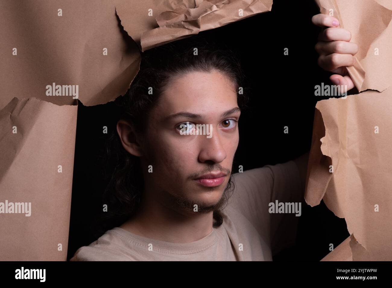 A man peering through a hole in a sheet of brown paper. Tearing the ...