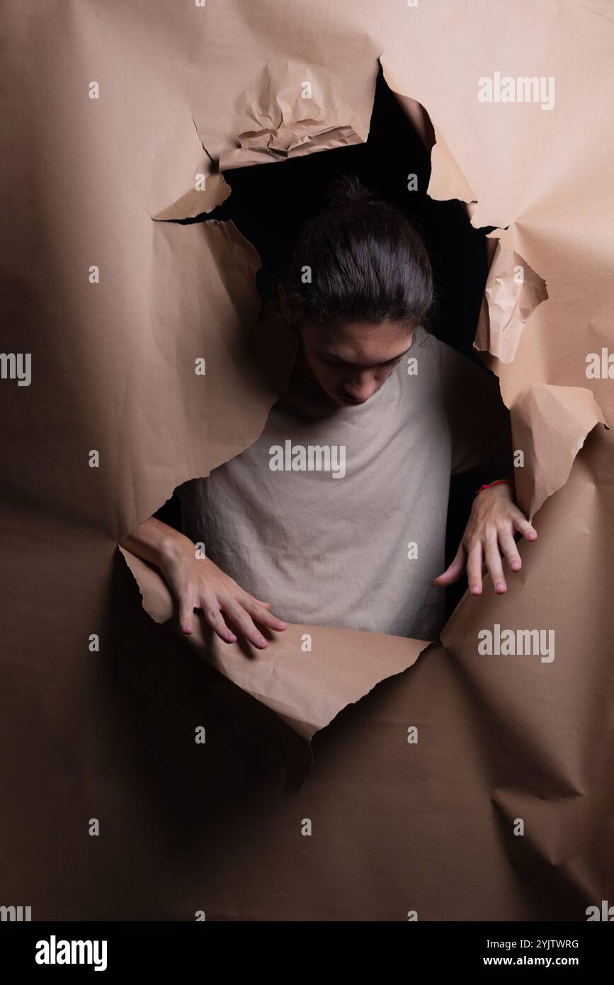 A man peering through a hole in a sheet of brown paper. Tearing the ...