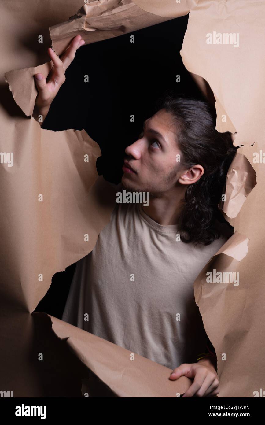 A man peering through a hole in a sheet of brown paper. Tearing the ...