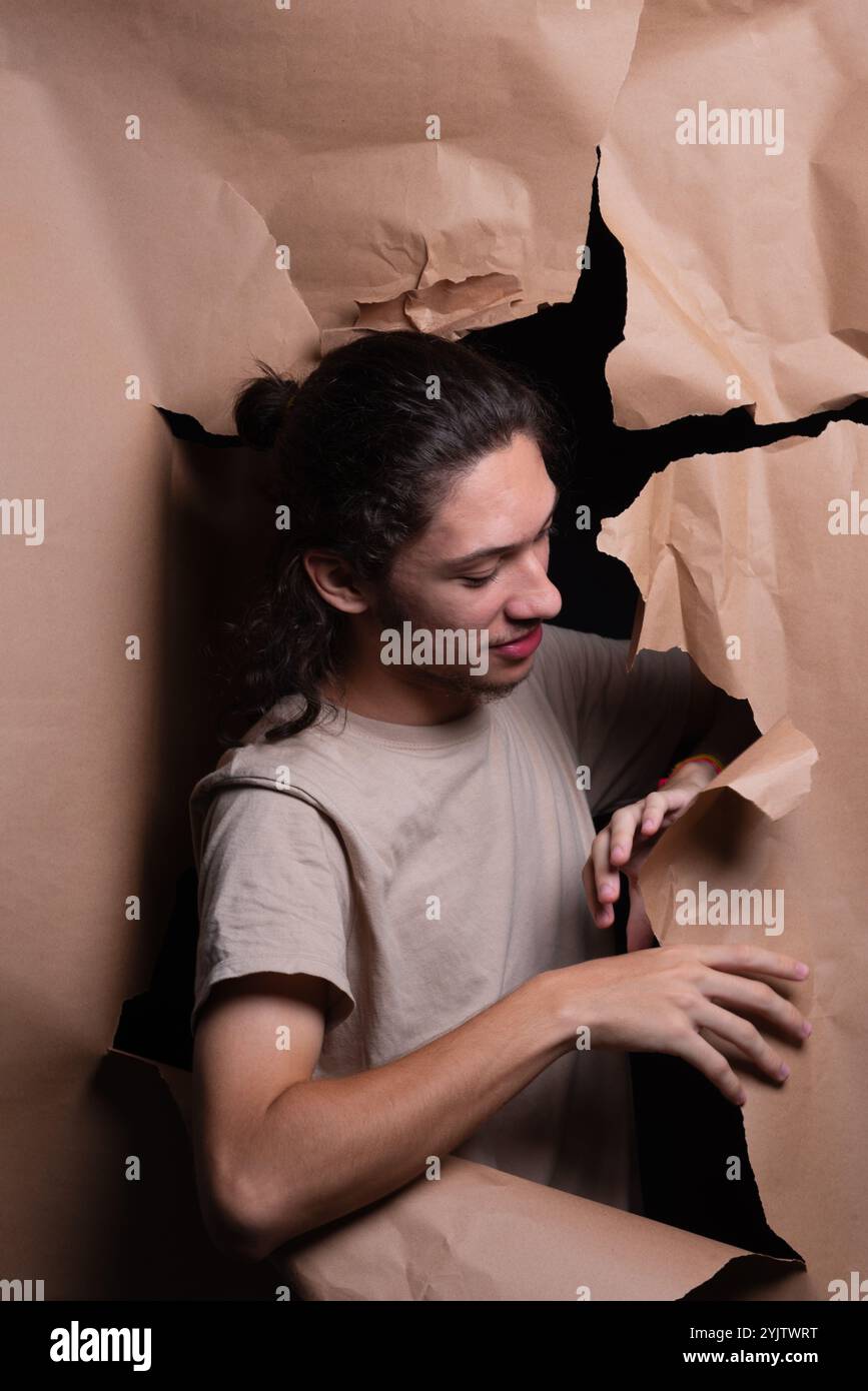 A man peering through a hole in a sheet of brown paper. Tearing the ...
