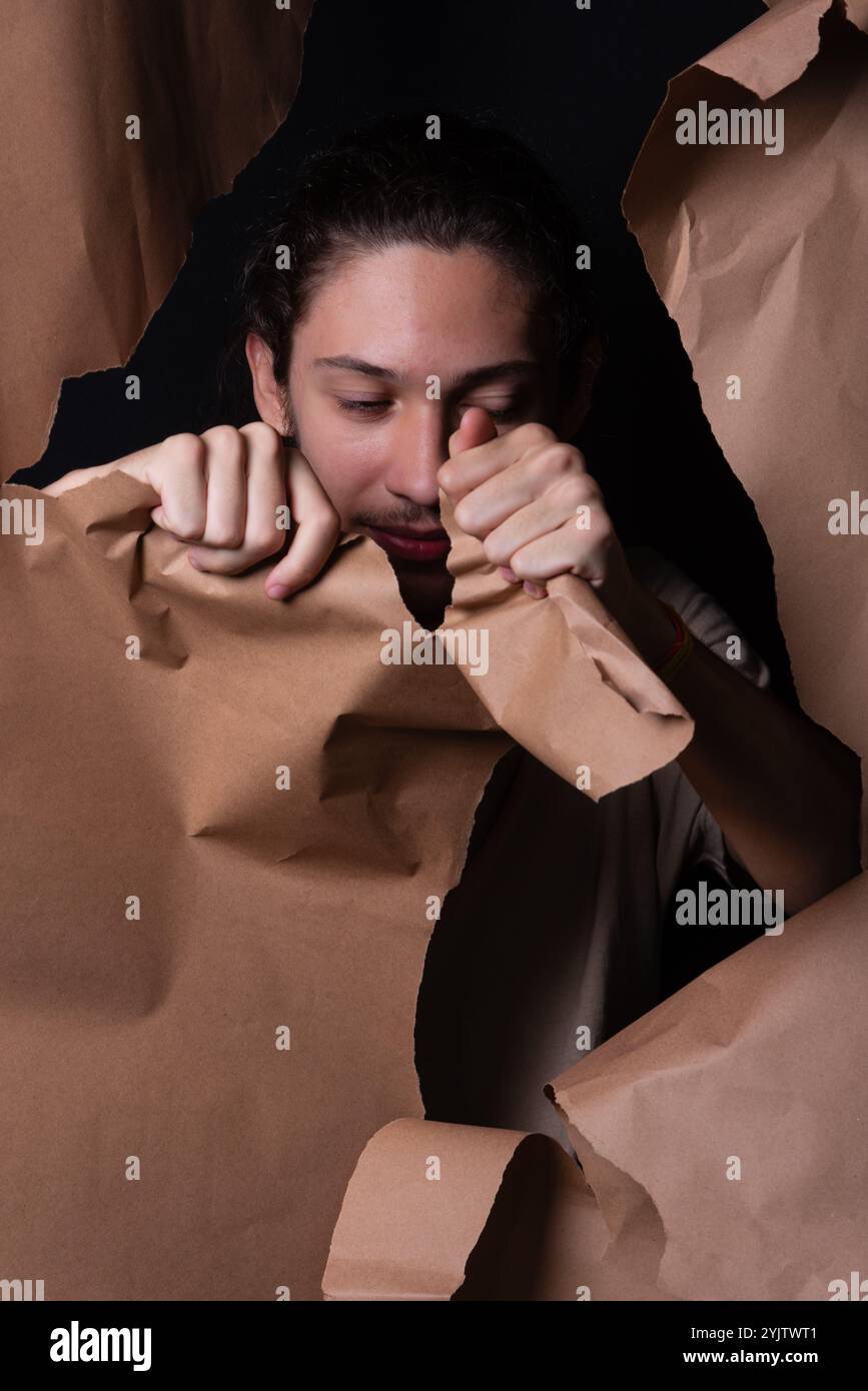A man peering through a hole in a sheet of brown paper. Tearing the ...