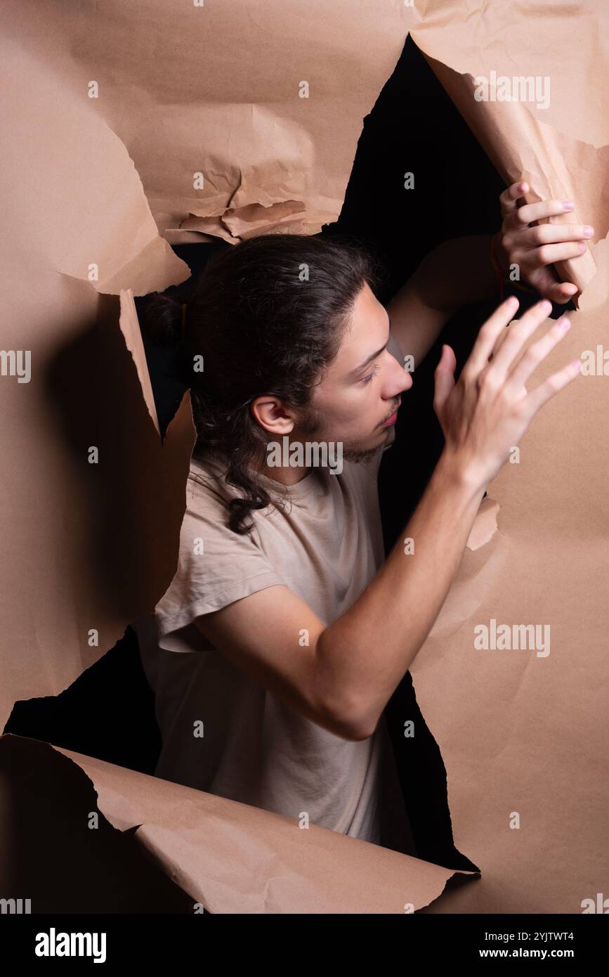 A man peering through a hole in a sheet of brown paper. Tearing the ...