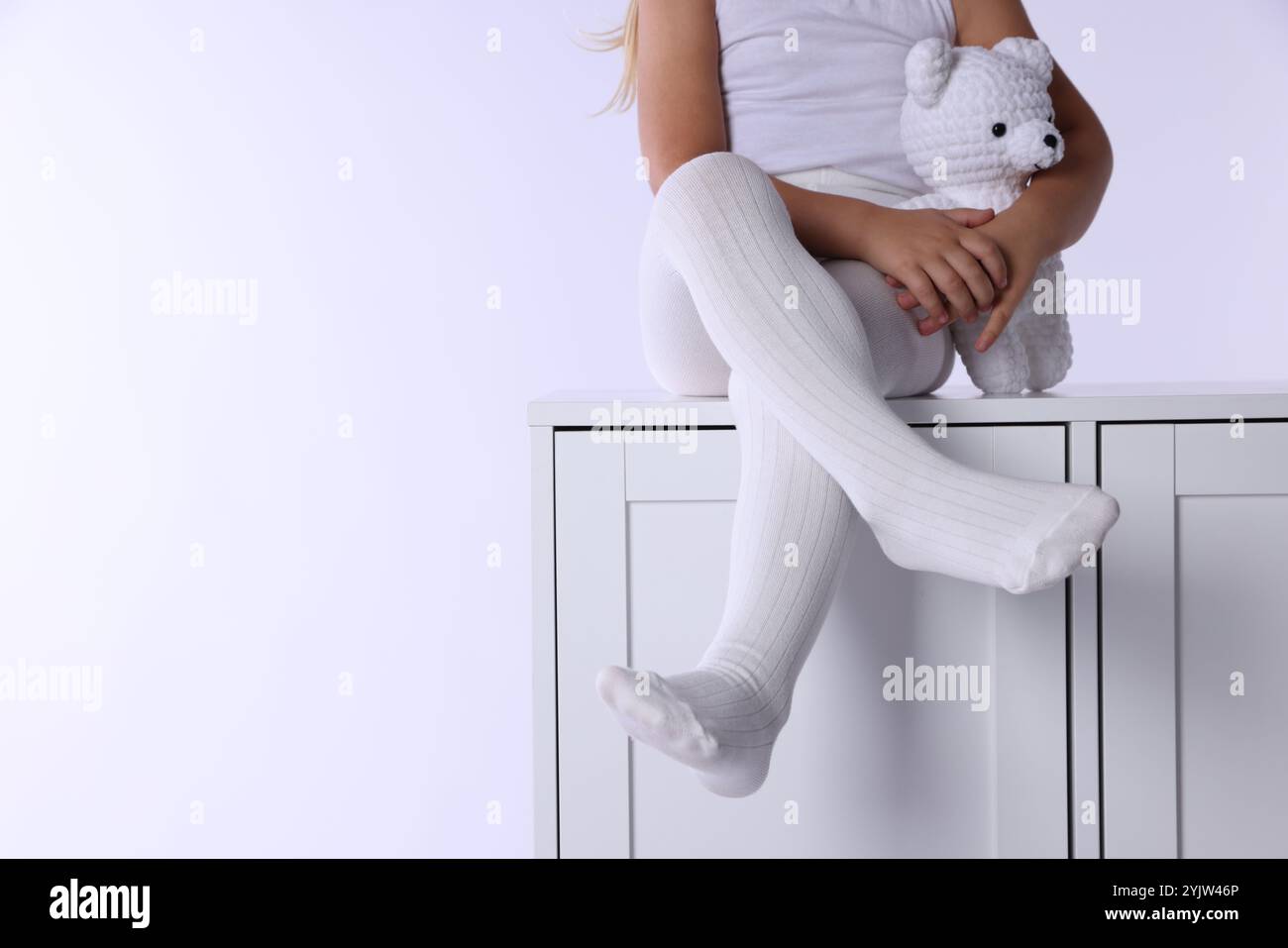 Child in tights sitting on cabinet against white background, closeup ...