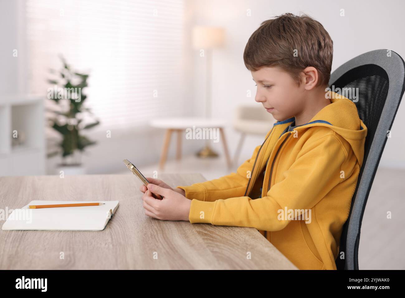 Boy with correct posture using smartphone at wooden desk indoors Stock ...