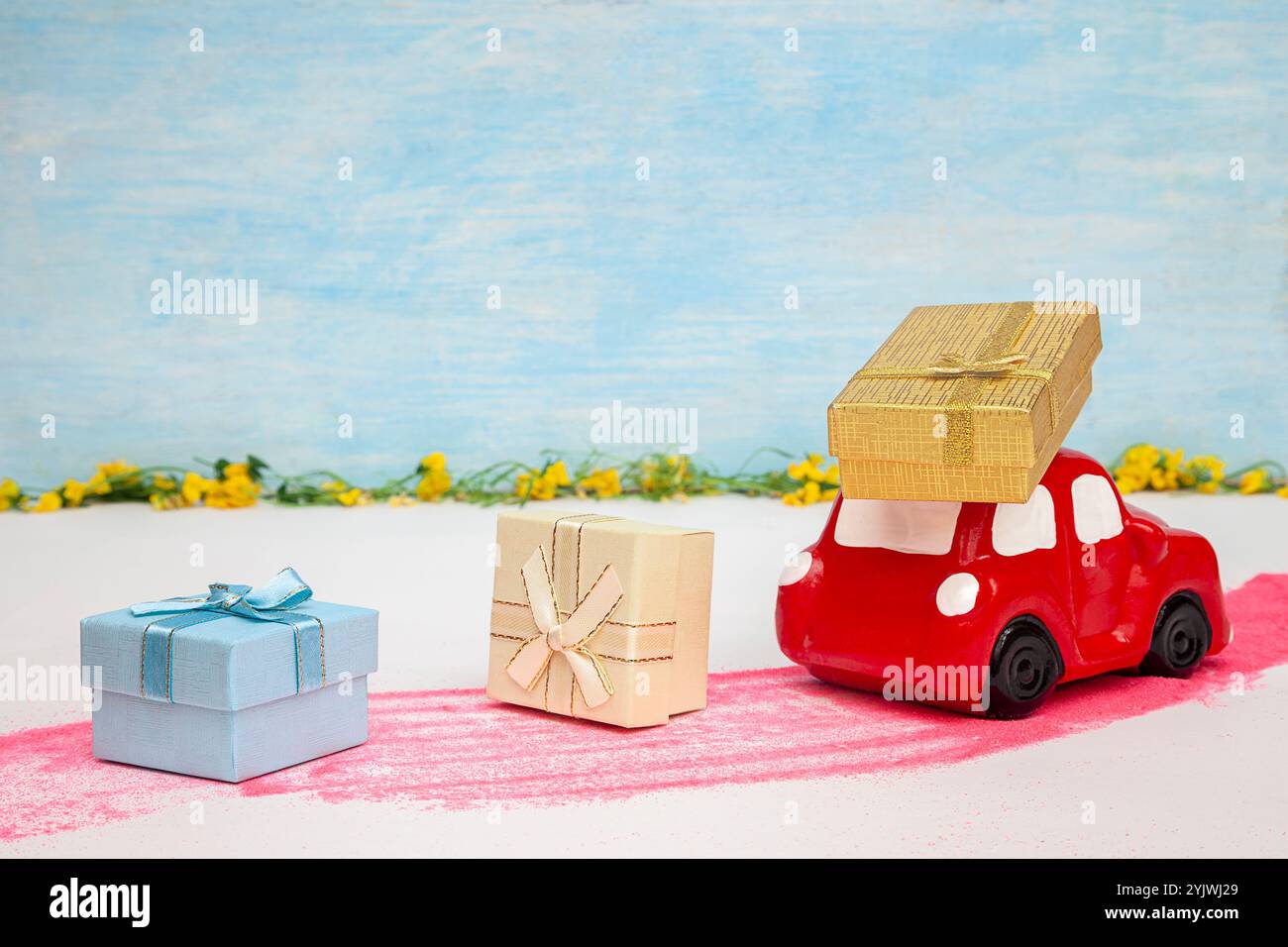 Gift boxes falling from red car on road with pink sand. Yellow flowers ...