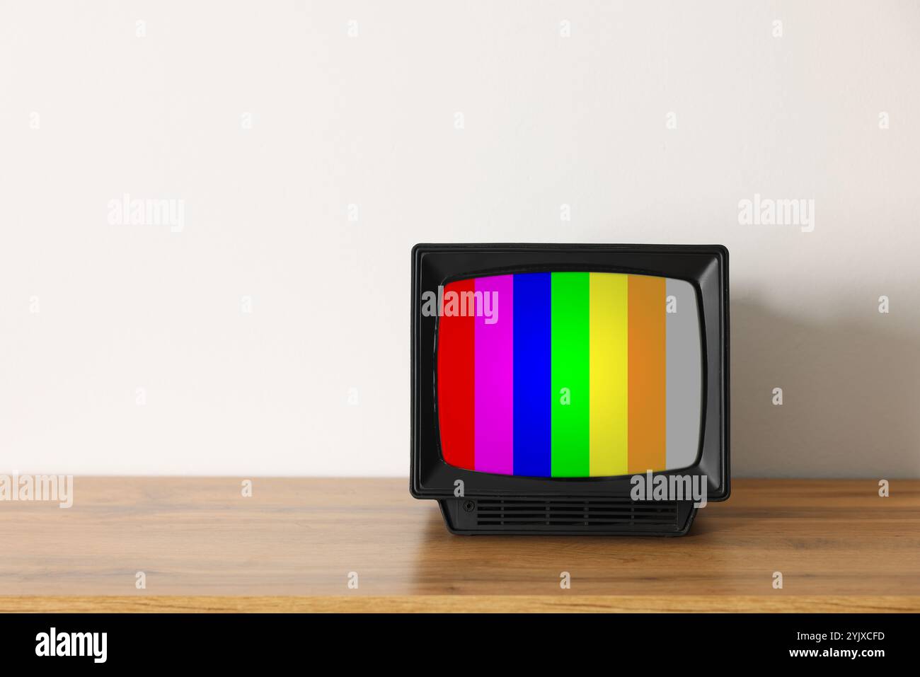 Retro TV set with test pattern on wooden table near white wall. Color ...