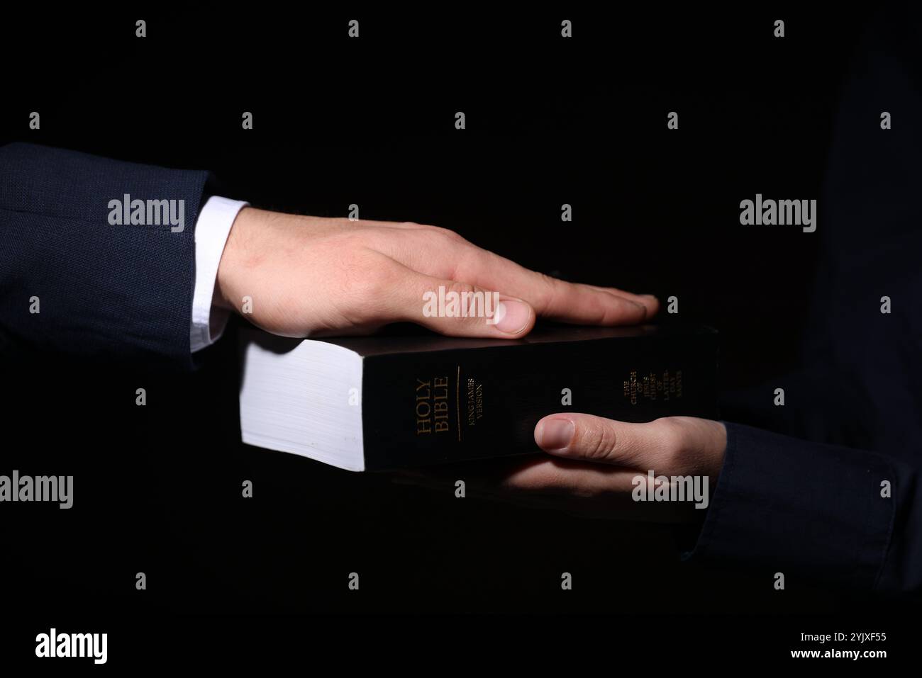 Man taking oath with his hand on Bible against black background ...