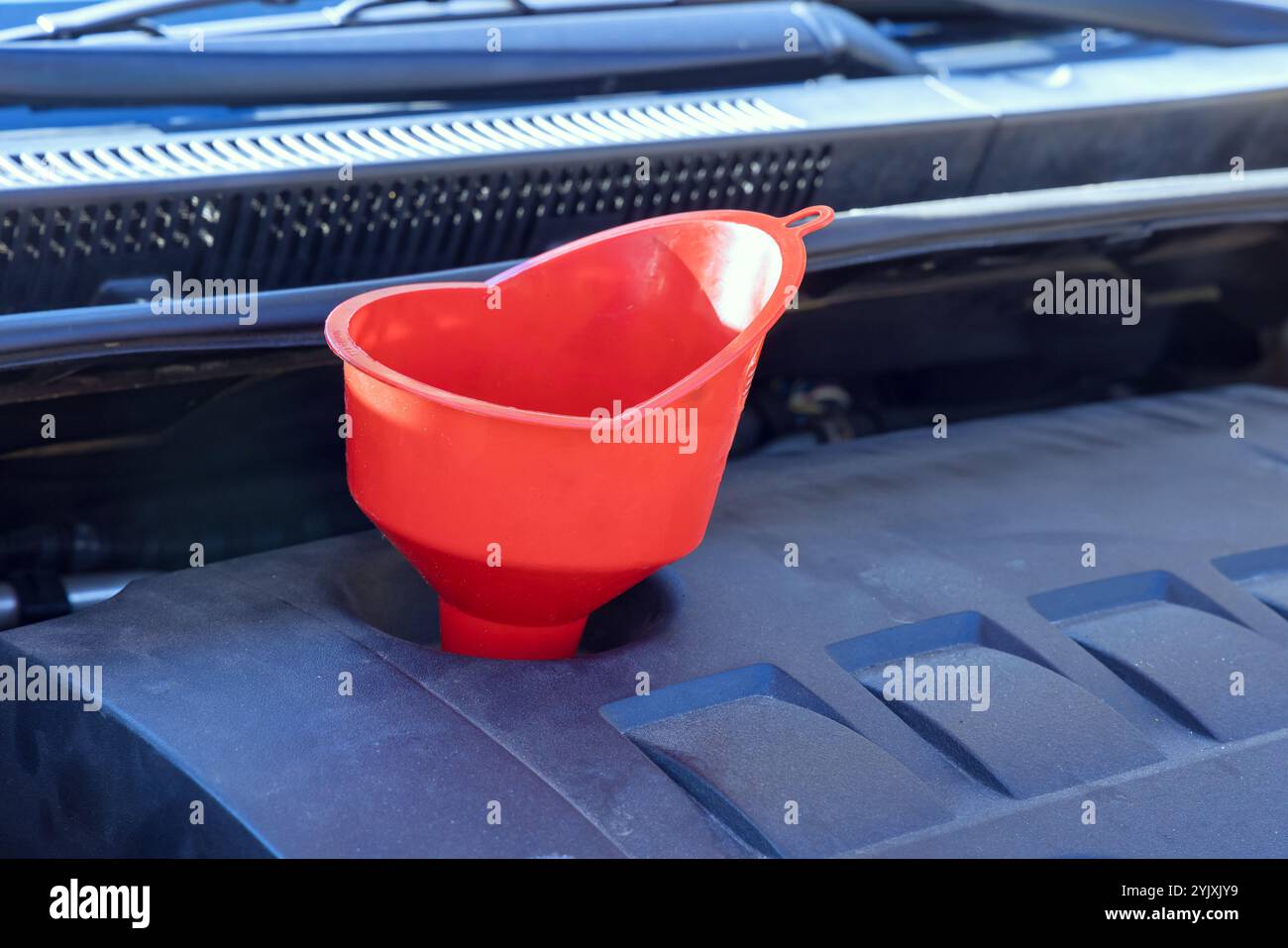 Bright red funnel rests on engine cover of vehicle while mechanic ...