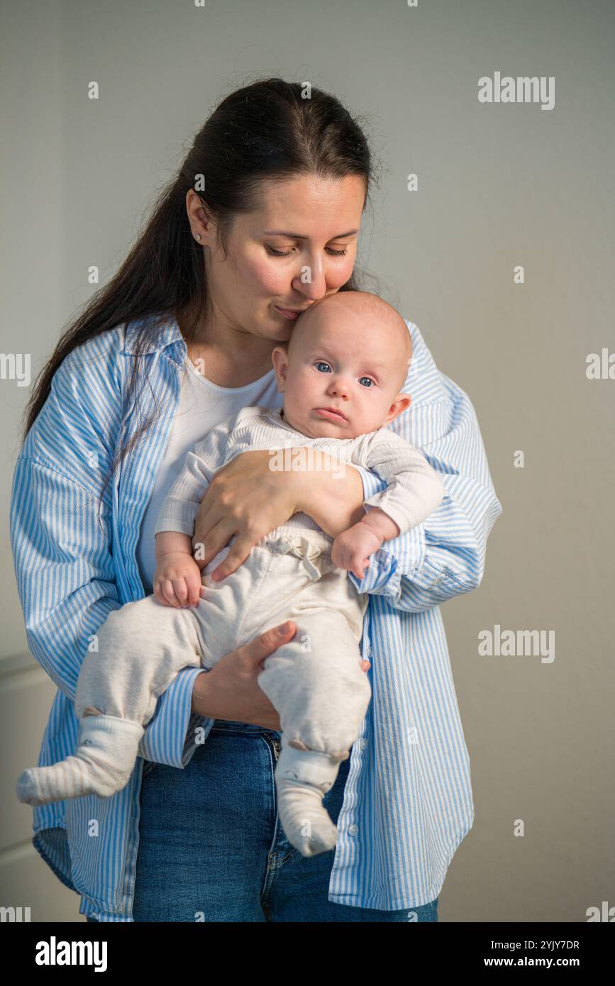 Affectionate mom holding a cute baby boy aged a few months and kissing ...