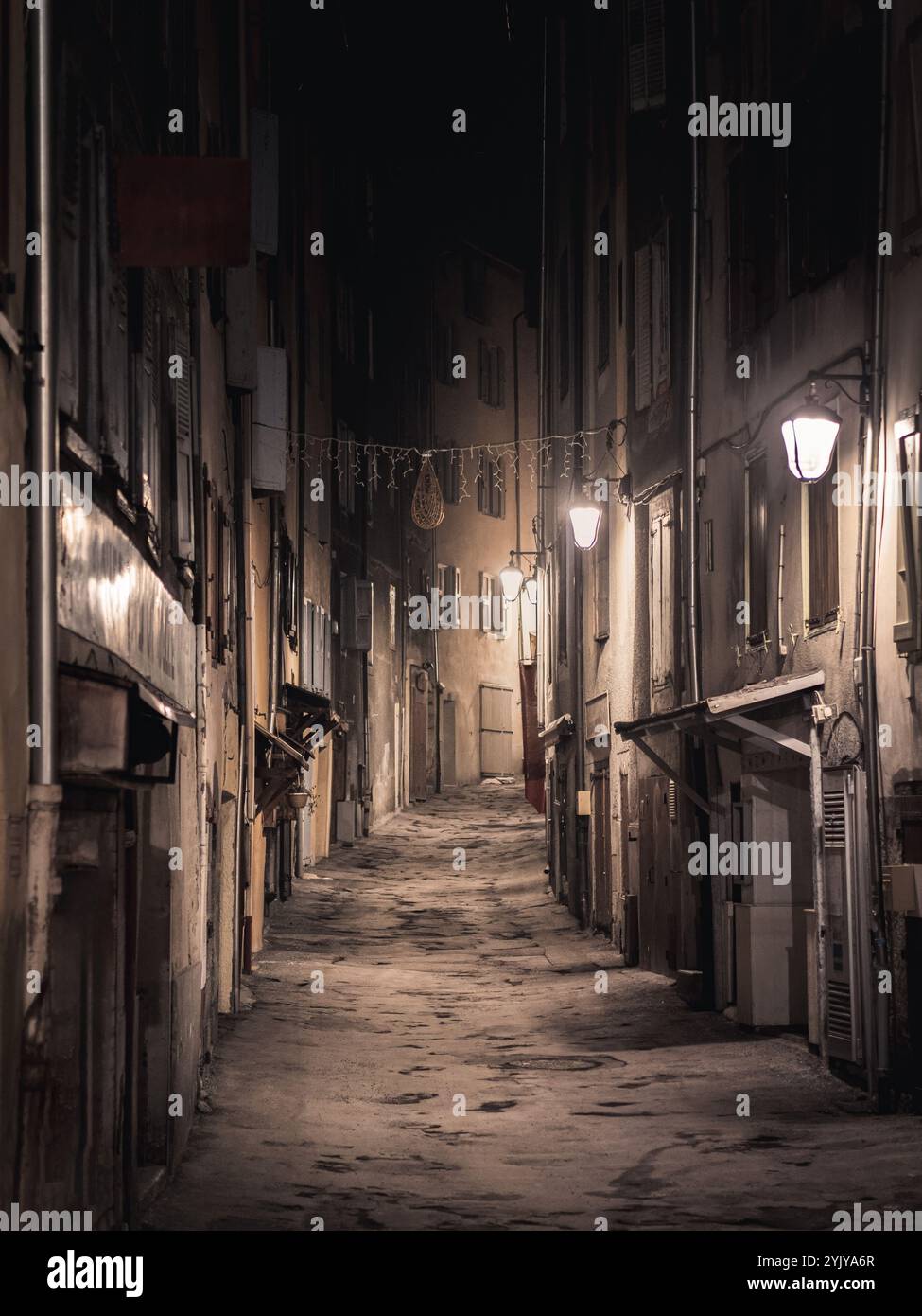 A dimly lit, narrow alleyway in Briançon, France, showcasing aged ...