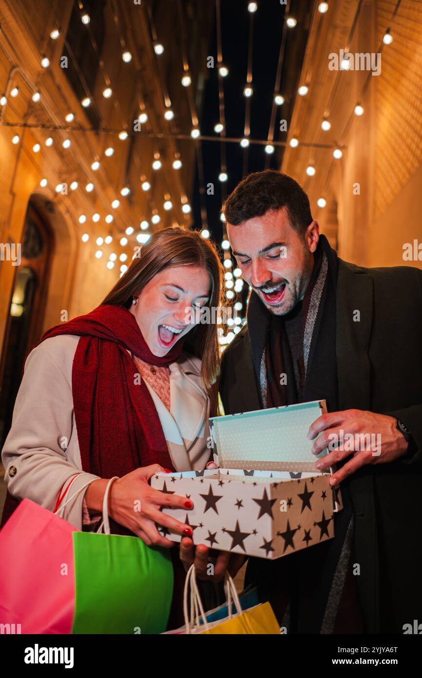 Vertical. Young couple unboxing a Christmas gift outdoors at night ...
