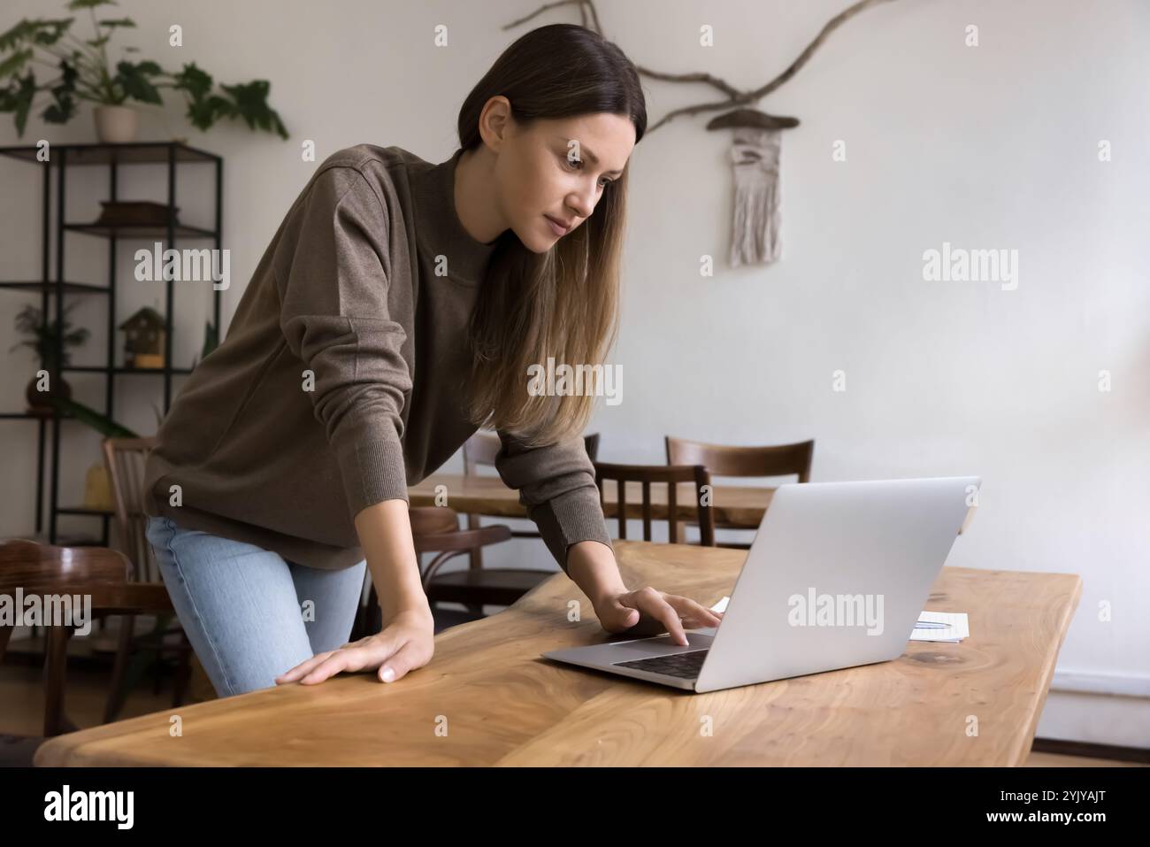 Woman standing at table, working on her laptop Stock Photo - Alamy