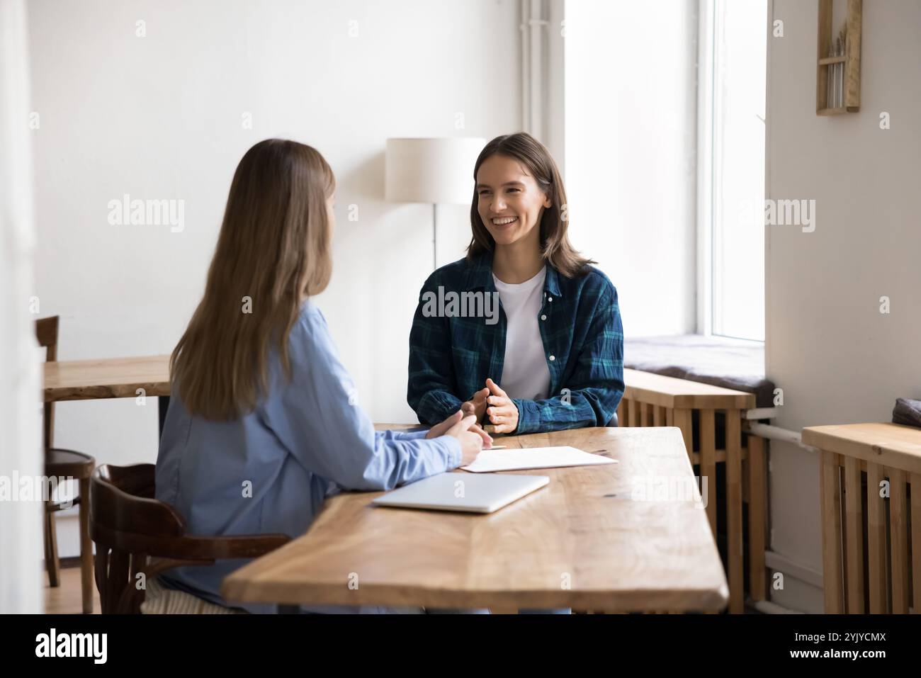 Two young women colleagues lead conversation seated at workplace desk ...