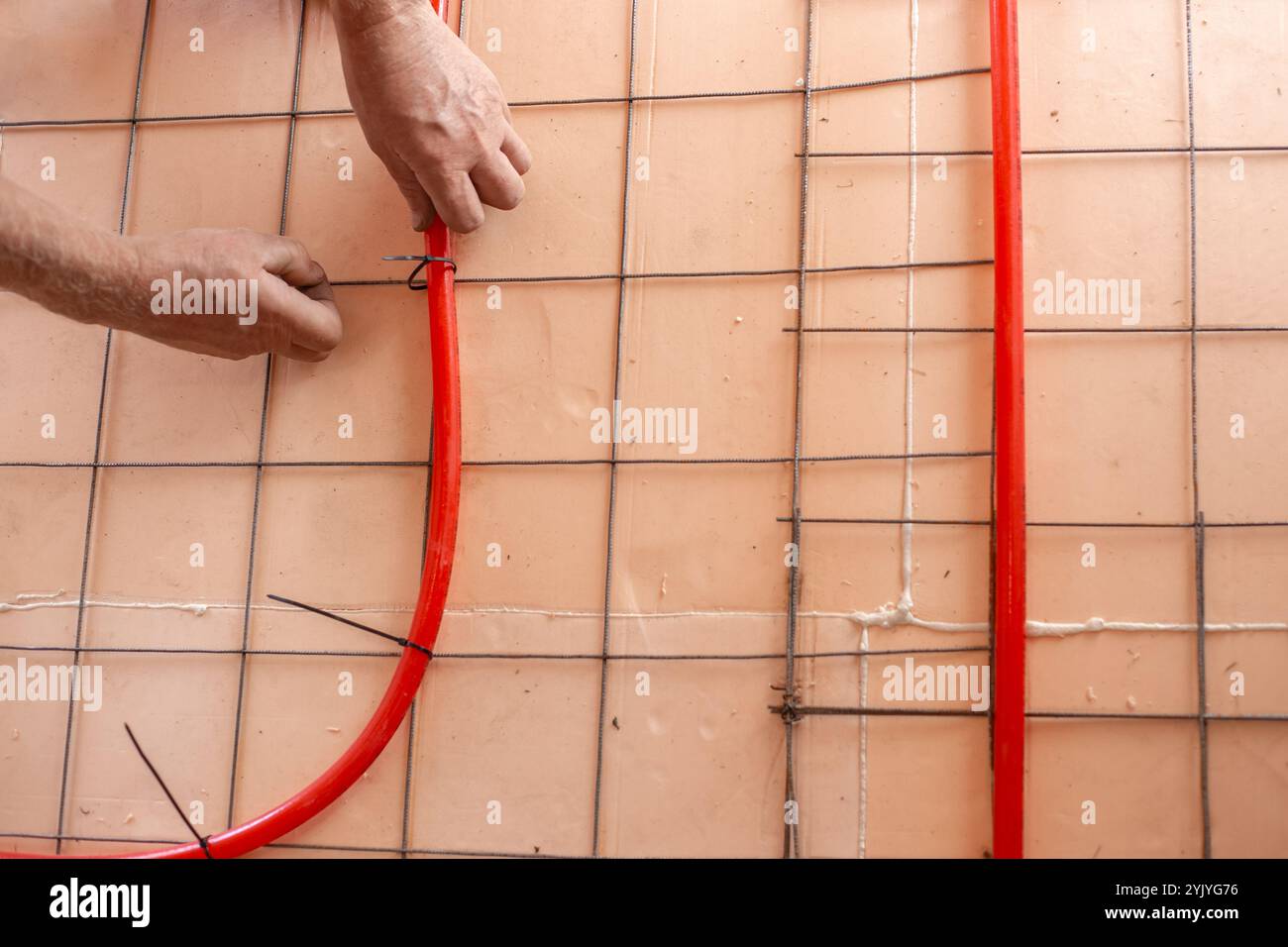 Installation of underfloor heating. A worker fastens pipes for ...