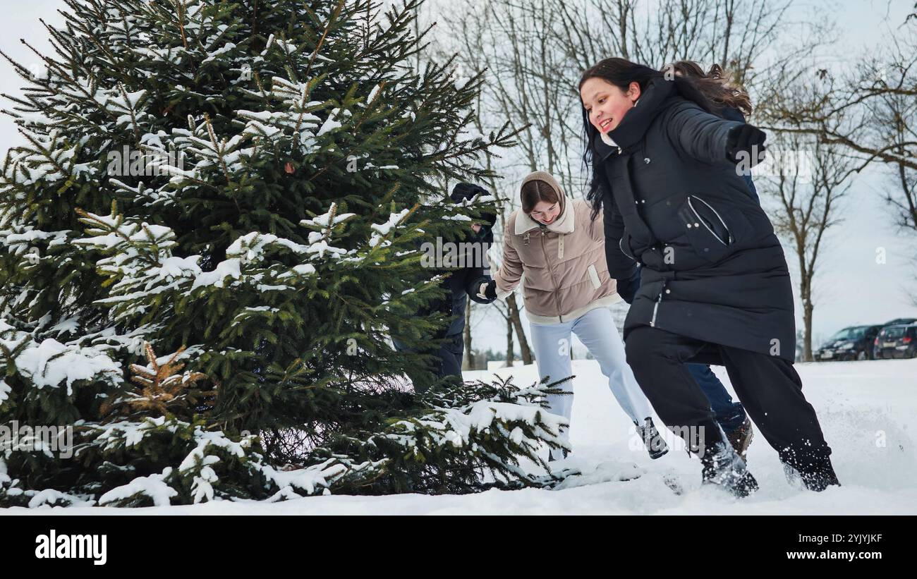 School friends run around the spruce tree holding hands. Christmas ...