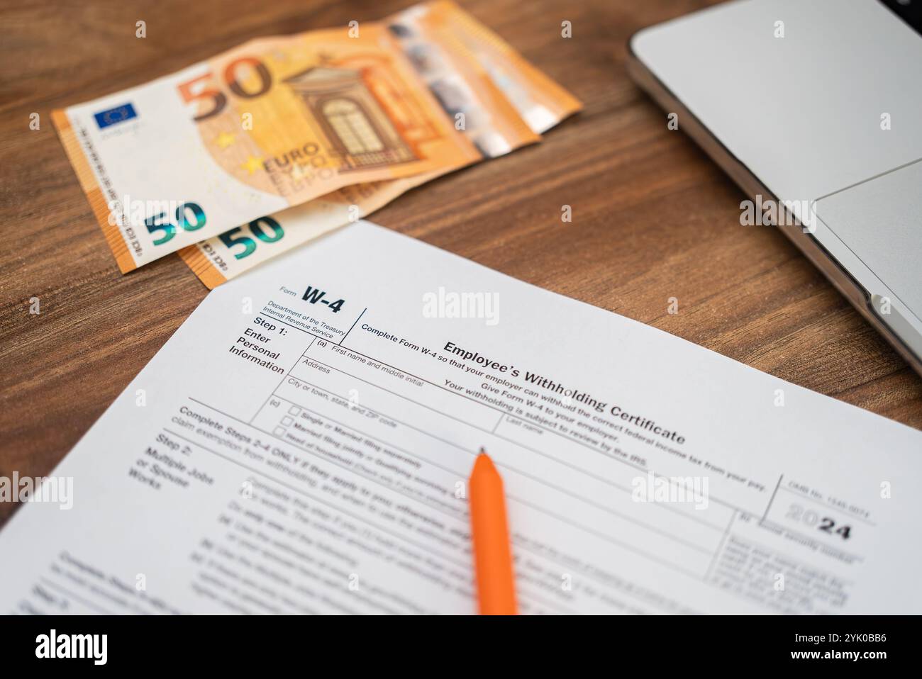 Employee filling out IRS form W-4 with euros and a laptop on a wooden ...