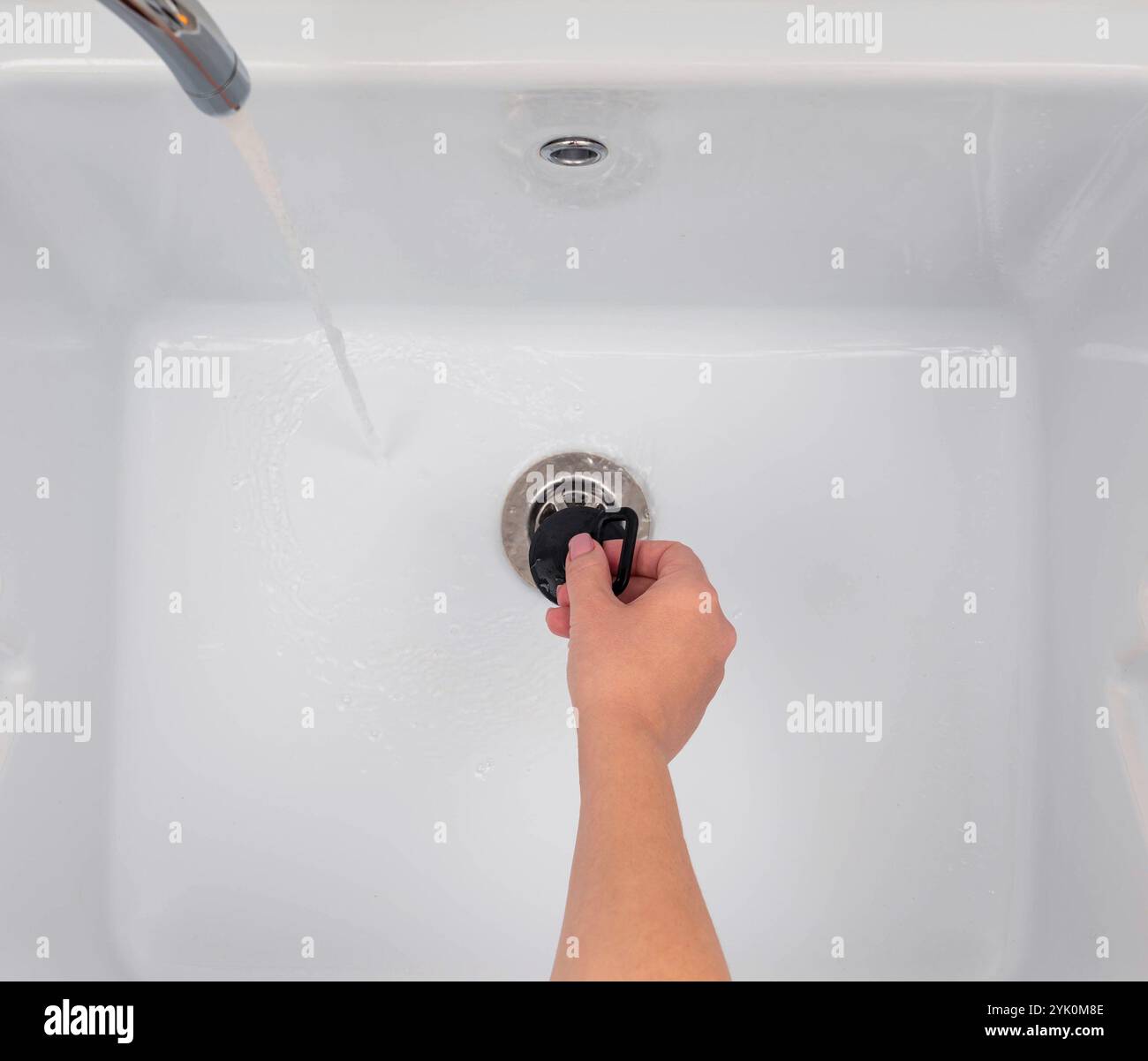 A person adjusting the drain plug in a utility sink with running water ...