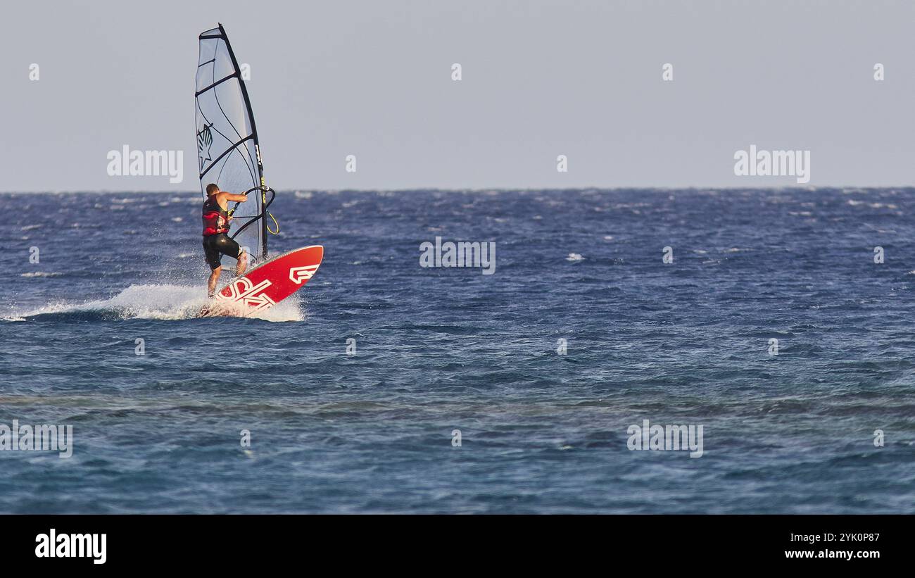 A windsurfer glides over the open sea with a red sail, windsurfer ...