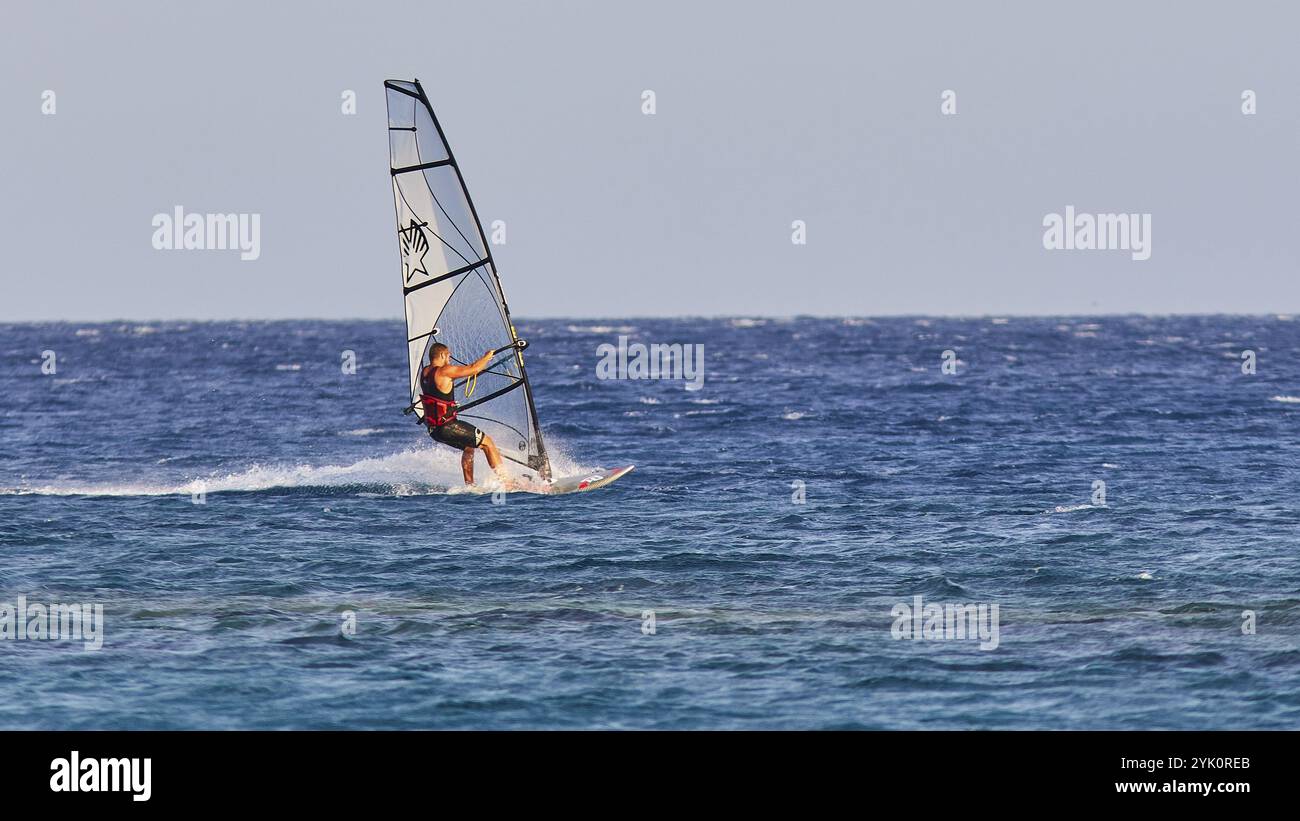 A windsurfer with a stylish sail glides over the sea surface ...