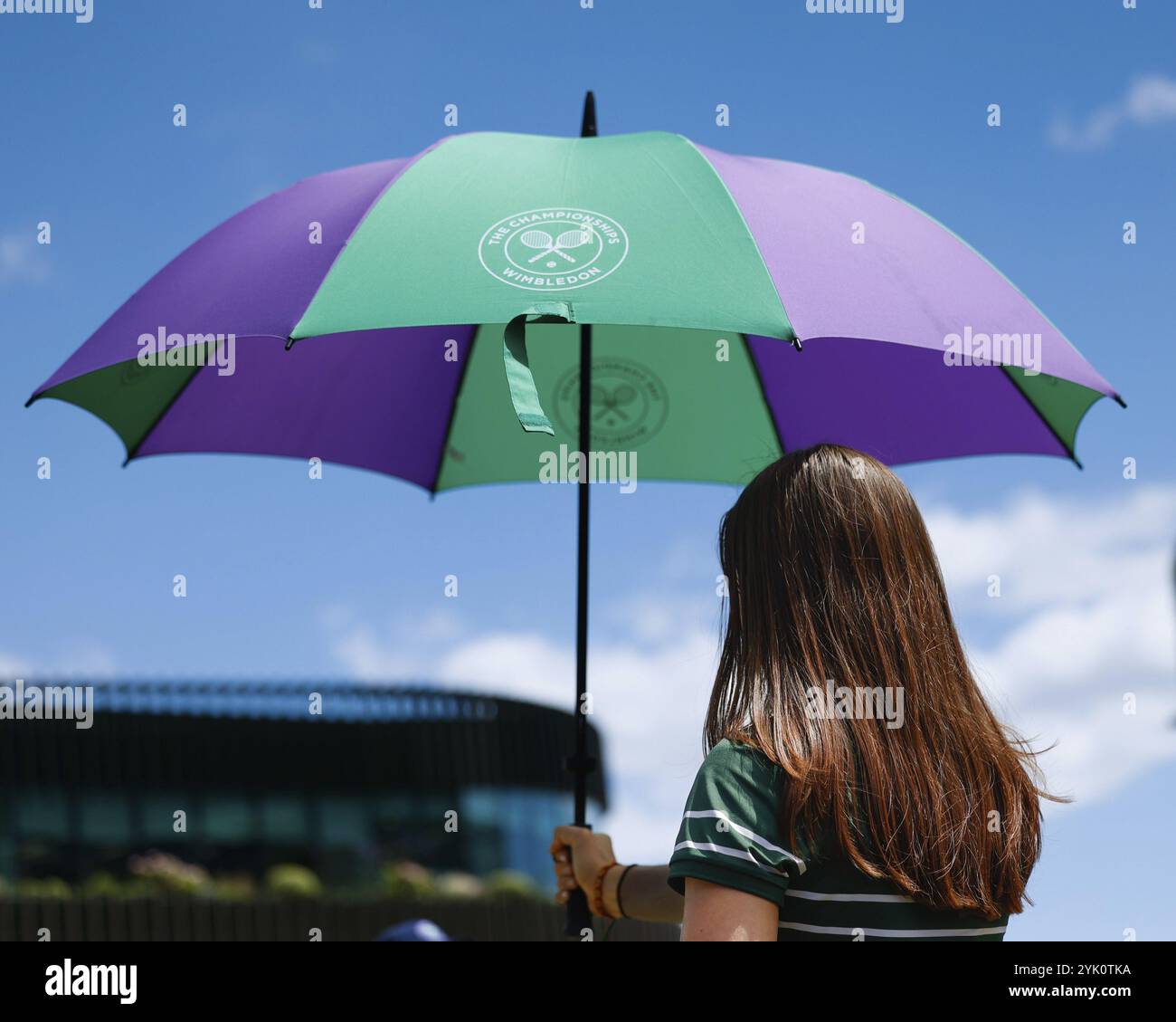 Longhaired girl holding umbrella to keep sunshine off player at the ...
