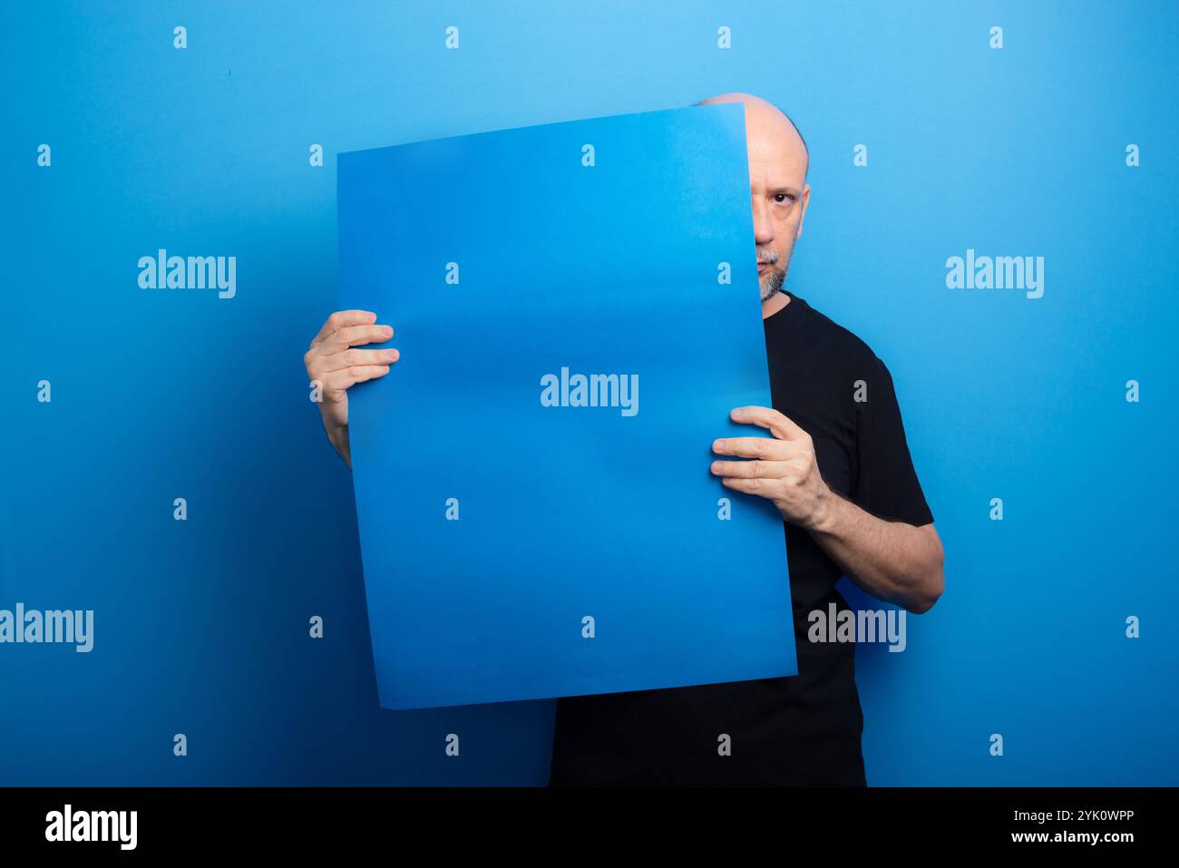 Bearded, bald man holding and hiding behind a blue colored poster ...