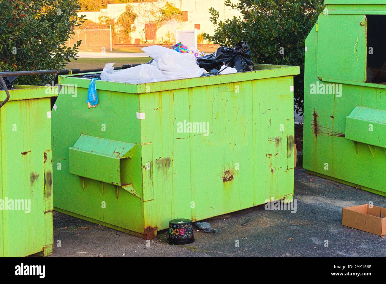 Community dumpsters in a parking lot are overflowing with trash bags ...