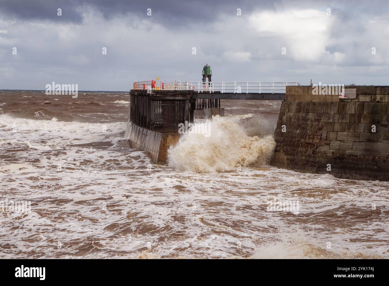 A large wave crashes through a gap in the breakwater of Whitby Harbour ...
