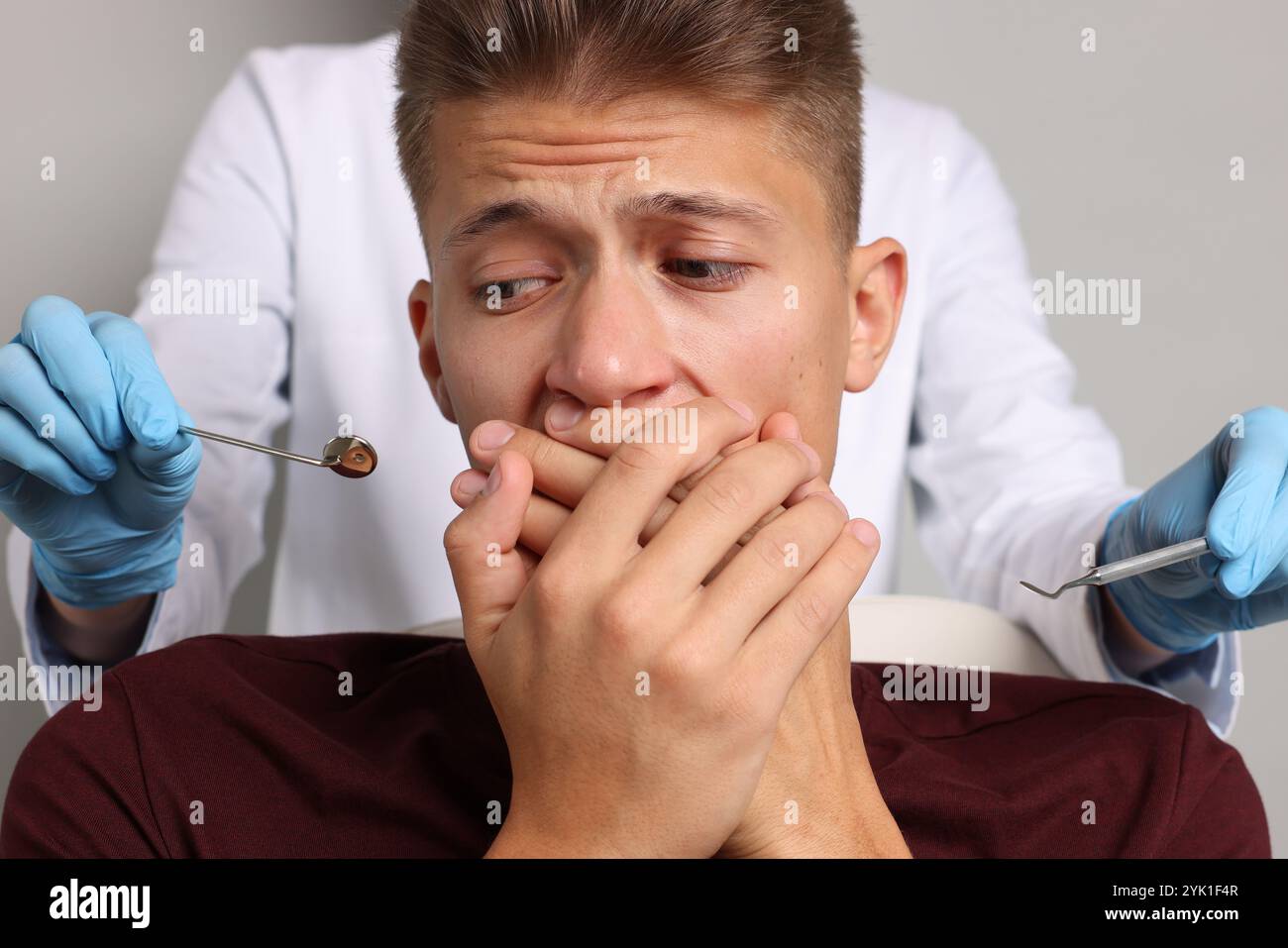 Dental phobia. Dentist working with scared man on grey background ...