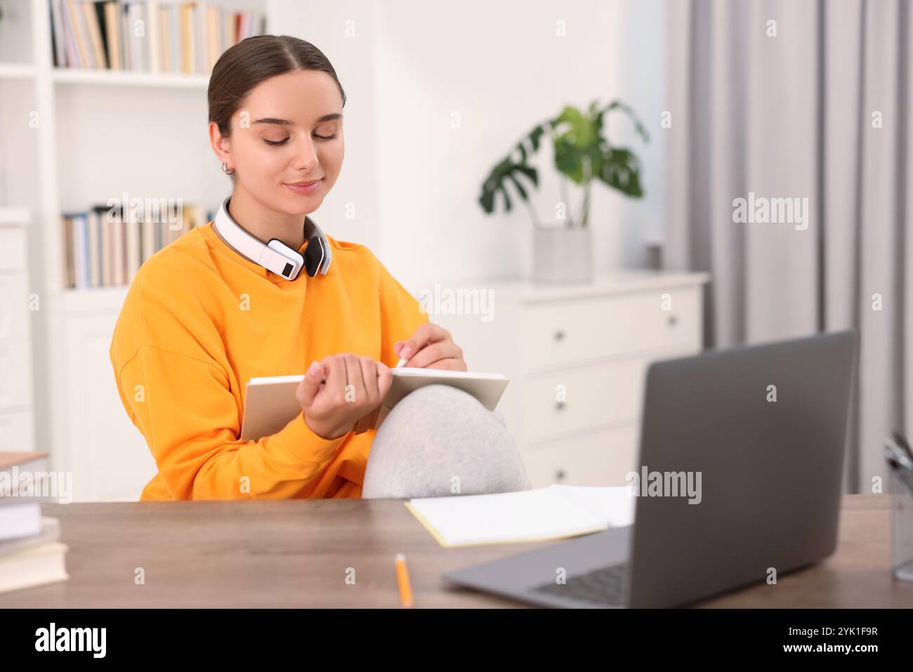 Student with headphones taking notes while studying indoors Stock Photo ...