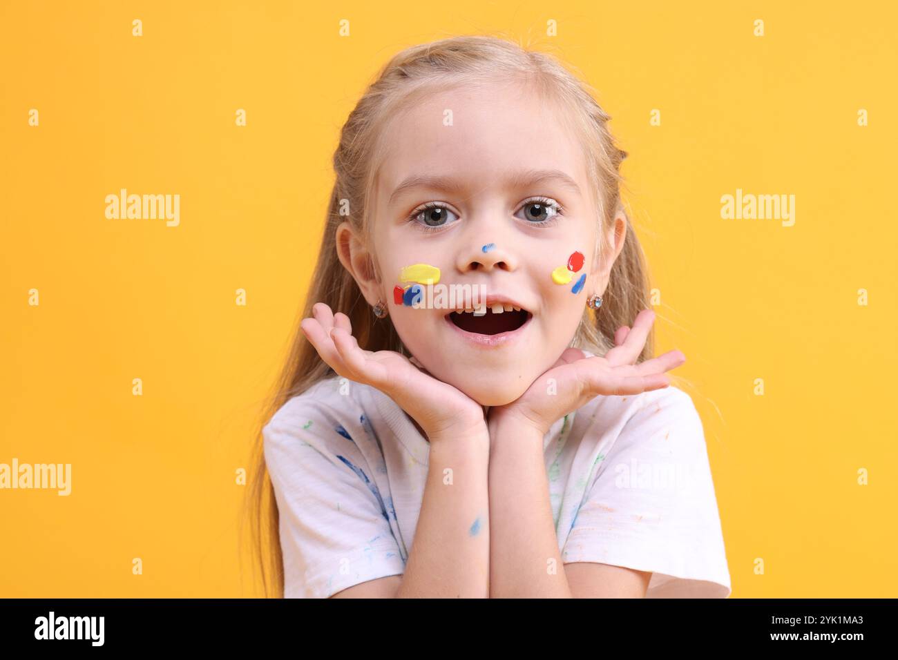 Portrait of cute girl smeared in paint on orange background. Space for ...