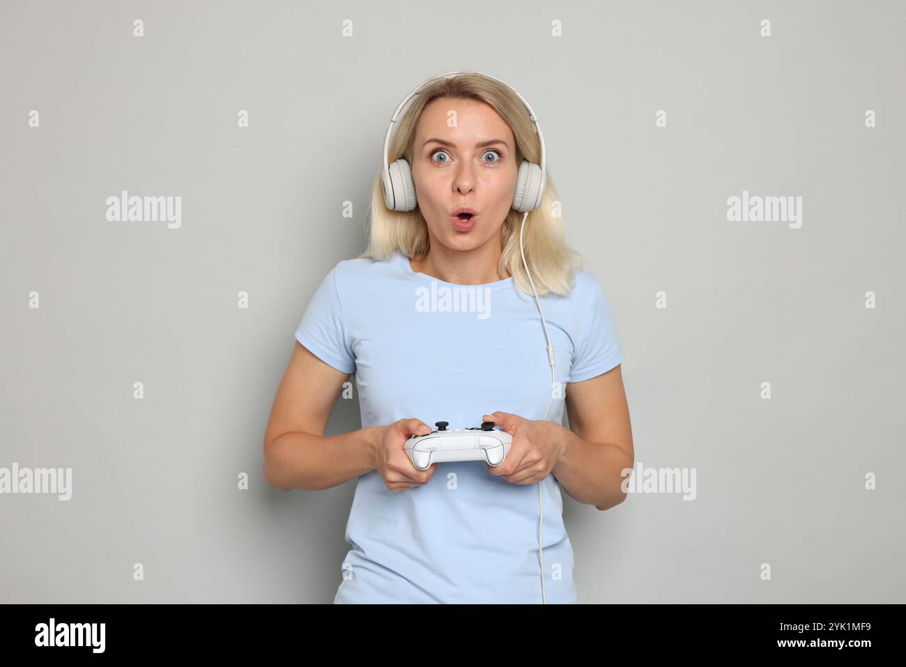 Surprised woman in headphones playing video games with controller on ...