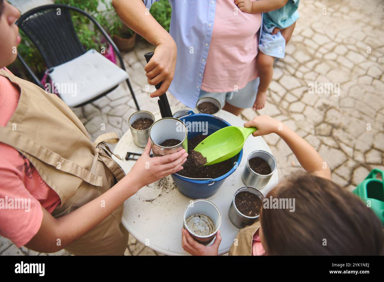 A family enjoys gardening by scooping soil into pots for planting. The ...