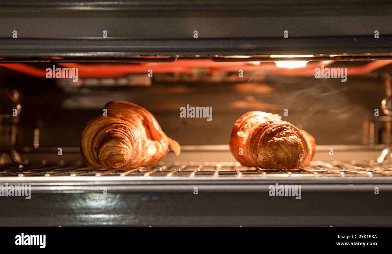 Two croissants baking in an oven with warm light illuminating the ...