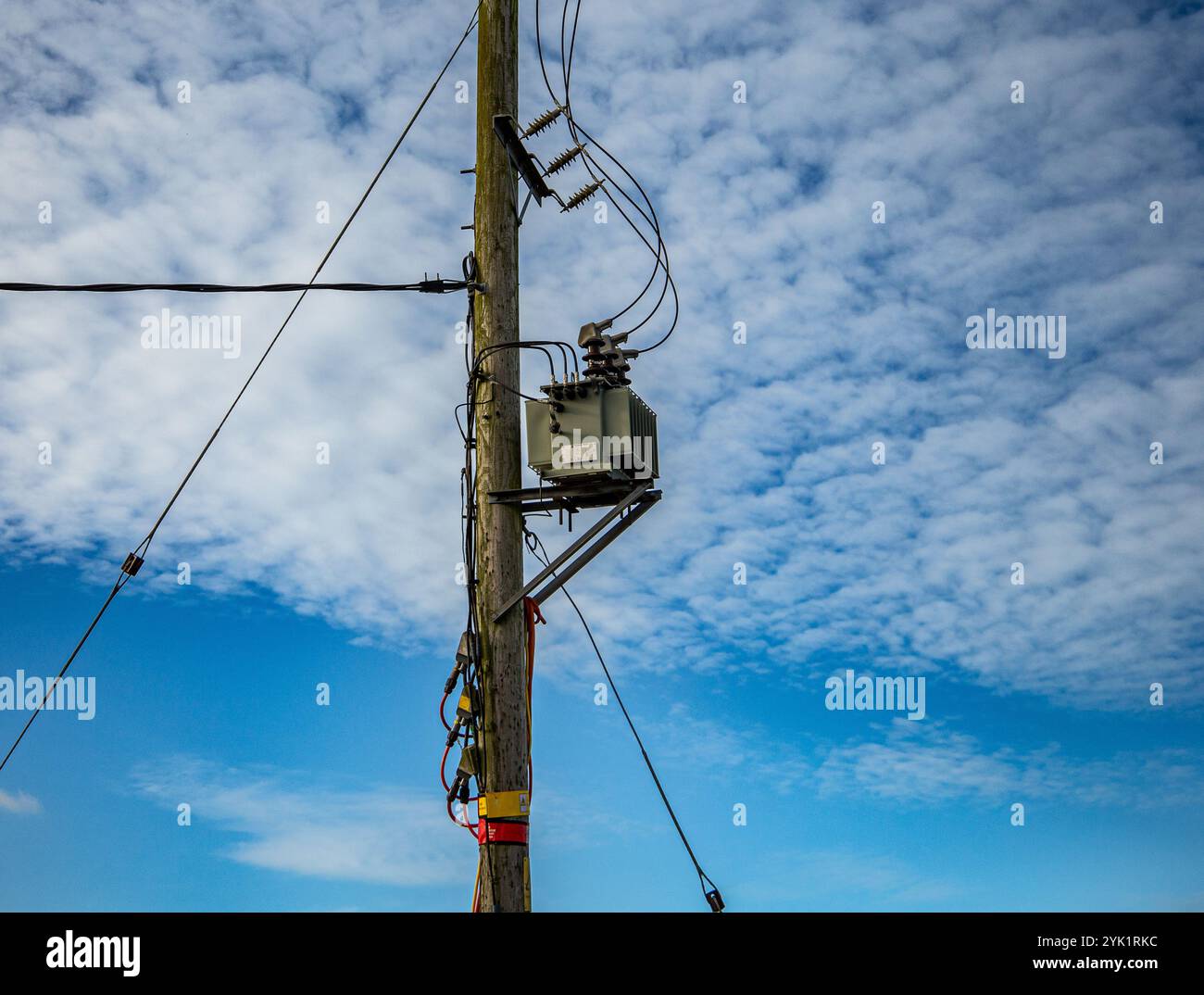 Electric utility pole with transformers and wires against a vibrant blue sky with scattered ...