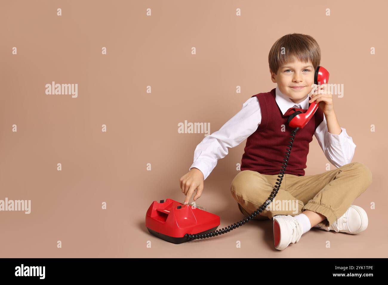 Cute little boy with old telephone on beige background, space for text ...