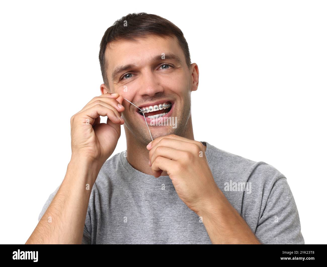 Man with braces cleaning teeth using dental floss on white background ...