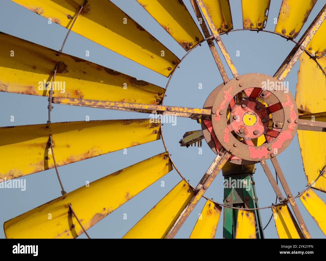 A vintage windmill with worn yellow blades rotates gently against a ...