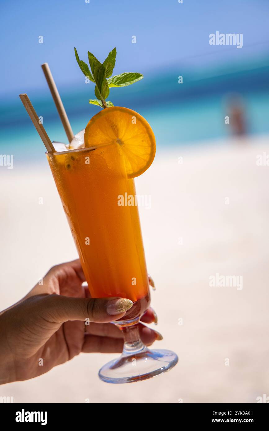 Detail of a colorful fruit cocktail in the hand of a woman on the beach ...