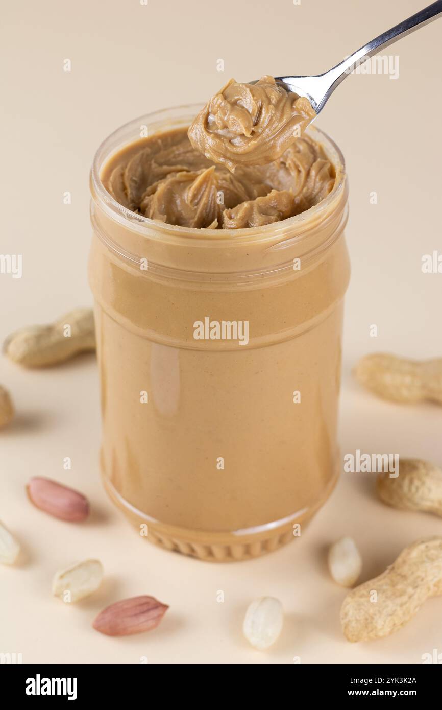 Open jar with crunchy peanut butter, peanut and a spoon on a beige ...