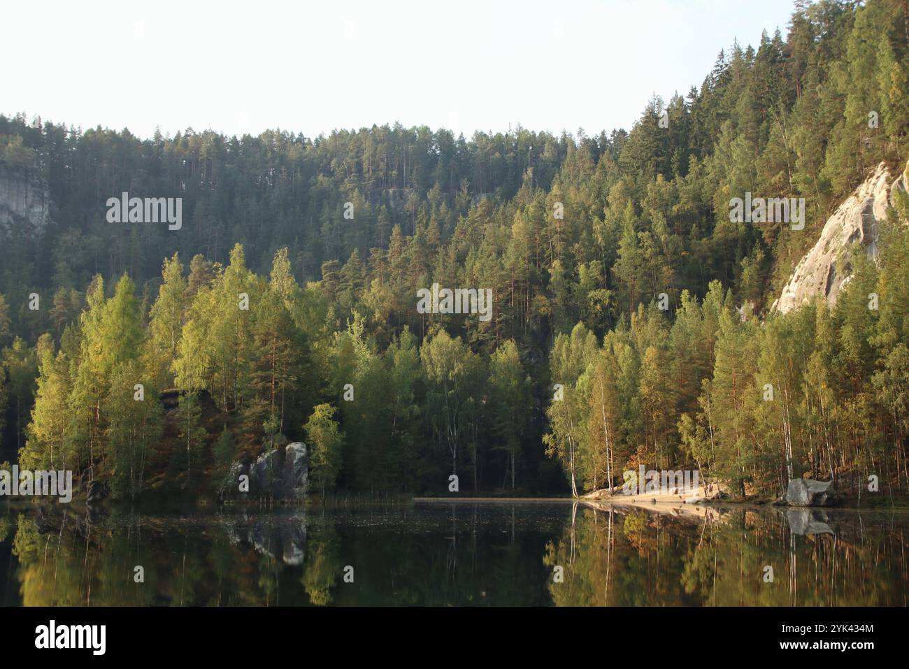 lake between rocks and woods at golden hour. Forests are reflected on ...